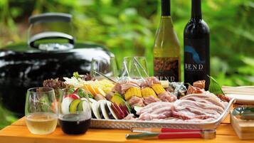 Um piquenique com diversos alimentos, bebidas e uma garrafa de vinho sobre uma mesa de madeira.