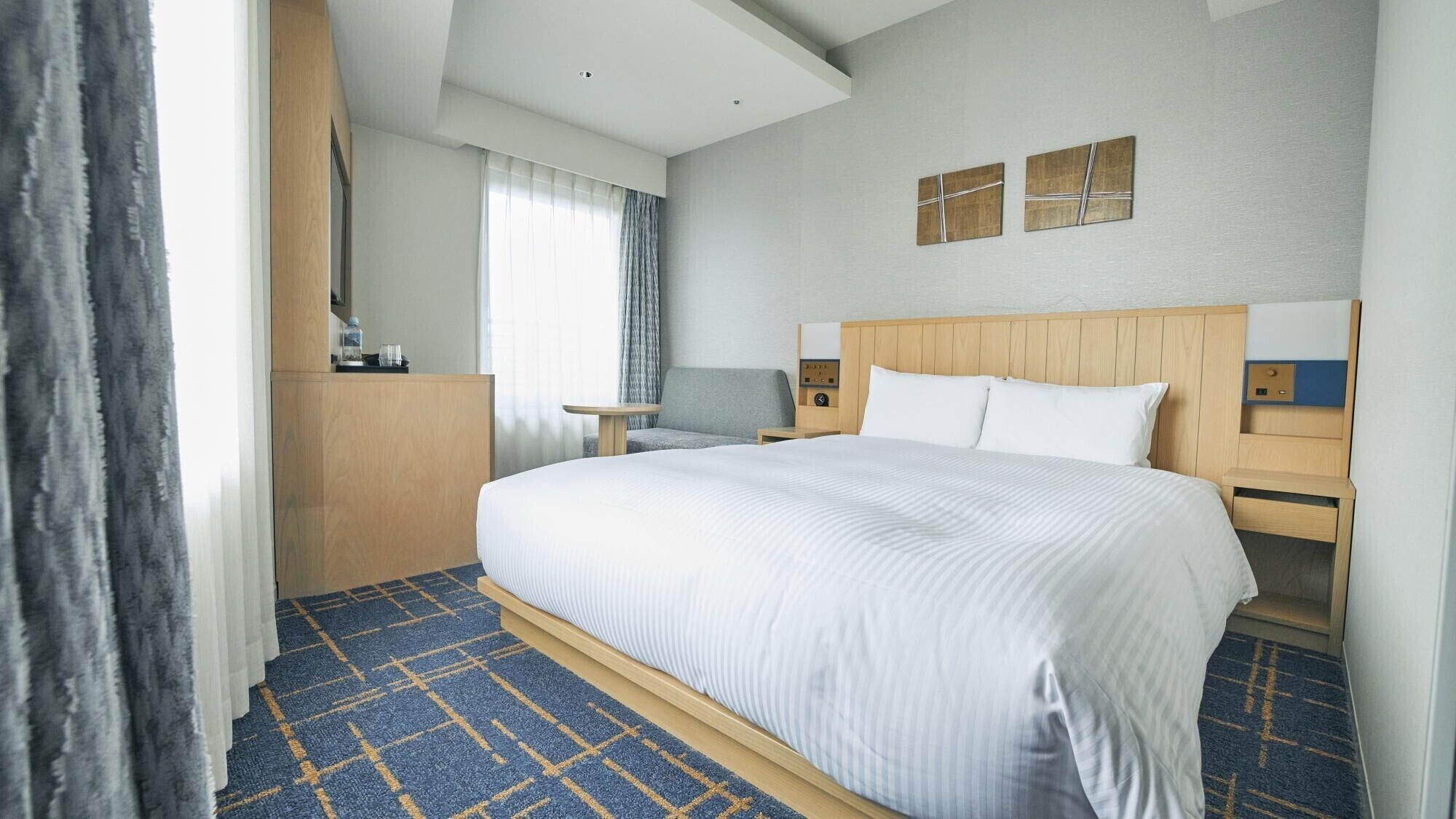 Quarto de hotel com cama, escrivaninha, cadeira, guarda-roupa e janela com cortinas.