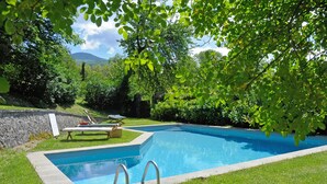Uma piscina retangular com borda de pedra, rodeada por grama e árvores.