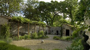 Um pátio rústico com paredes de pedra, caminho de cascalho e vegetação exuberante.