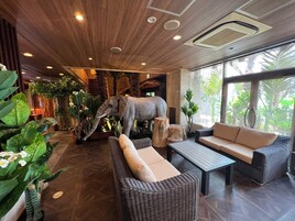 Um lobby espaçoso com uma grande estátua de elefante, móveis de vime e plantas tropicais.