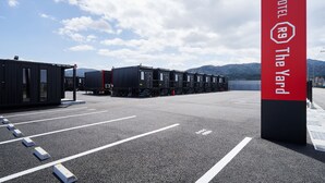Estacionamento de hotel com vários contêineres de transporte e uma placa vermelha destacada com o nome do hotel.