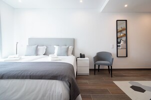 Quarto de hotel moderno com uma cama grande, uma mesa de cabeceira, uma cadeira e um espelho na parede.