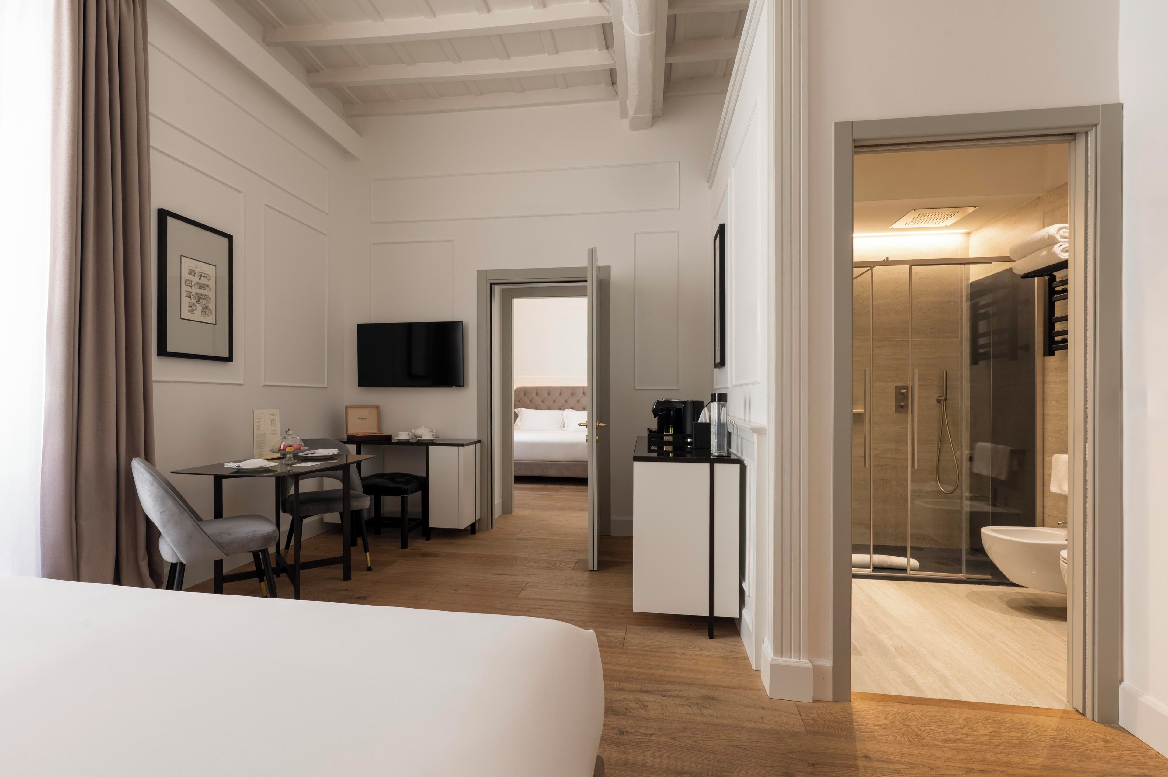 Quarto de hotel com cama, escrivaninha, cadeira, televisão e banheiro com chuveiro e vaso sanitário.