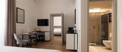 Quarto de hotel com cama, escrivaninha, cadeira, televisão e banheiro com chuveiro e vaso sanitário.