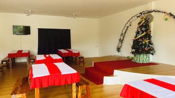 Um salão com várias mesas cobertas por toalhas vermelhas e brancas, um pinheiro de Natal e ventiladores de teto.