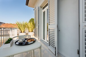 Varanda com mesa posta para dois, com bandeja de pães e café.