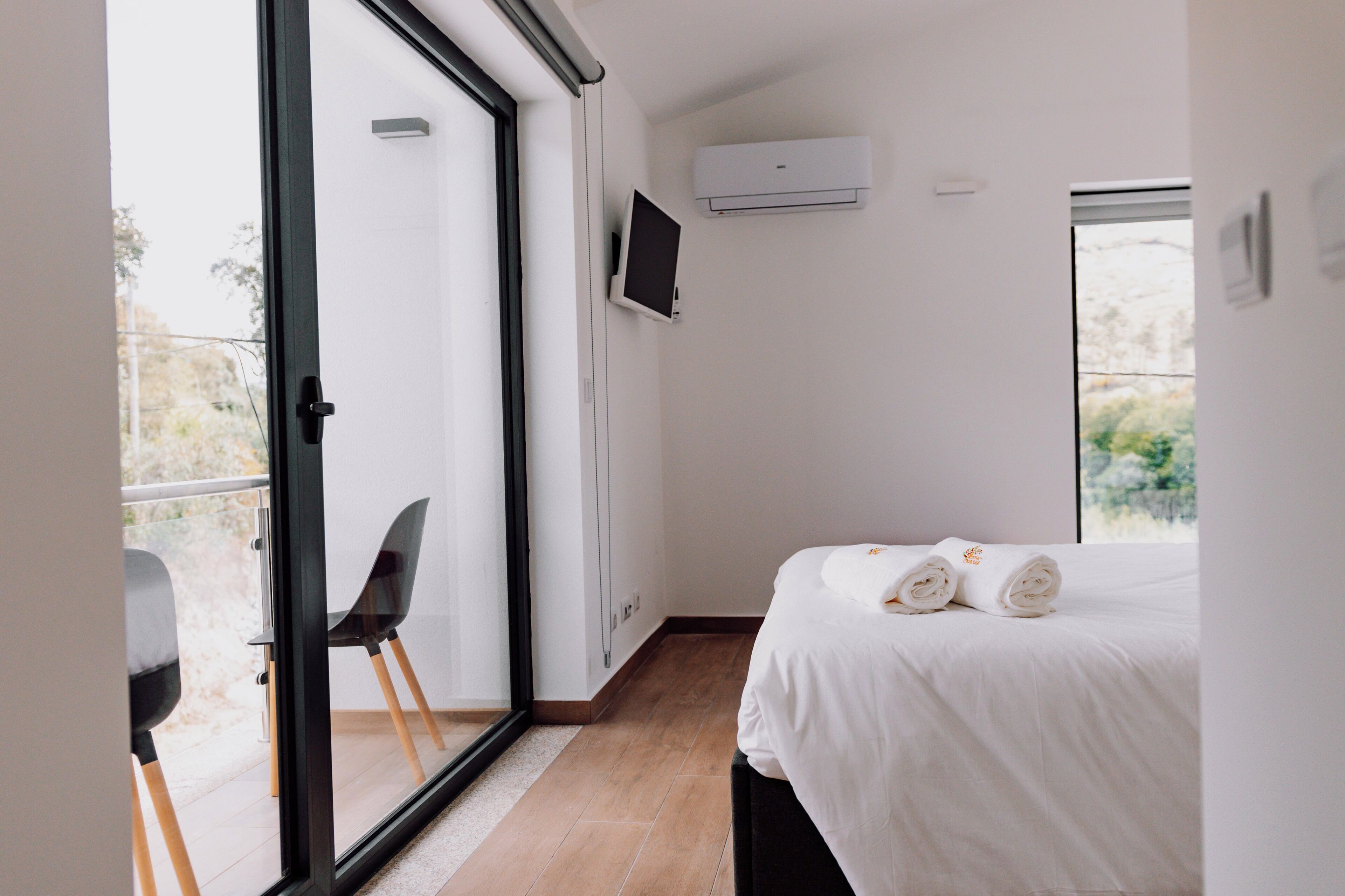 Quarto de hotel moderno com cama, televisão fixada na parede e porta de vidro deslizante para área externa.