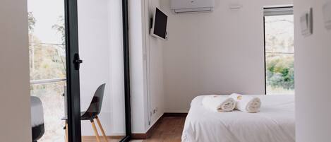 Quarto de hotel moderno com cama, televisão fixada na parede e porta de vidro deslizante para área externa.