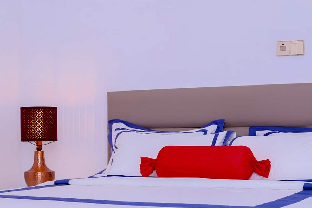 Uma cama bem arrumada com roupa de cama azul e branca, um travesseiro vermelho e um abajur decorativo.