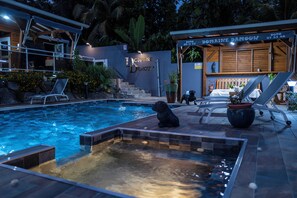 Uma área de piscina com hidromassagem, espreguiçadeiras e uma escadaria que leva a uma estrutura de madeira com a inscrição "Domaine Damouw".