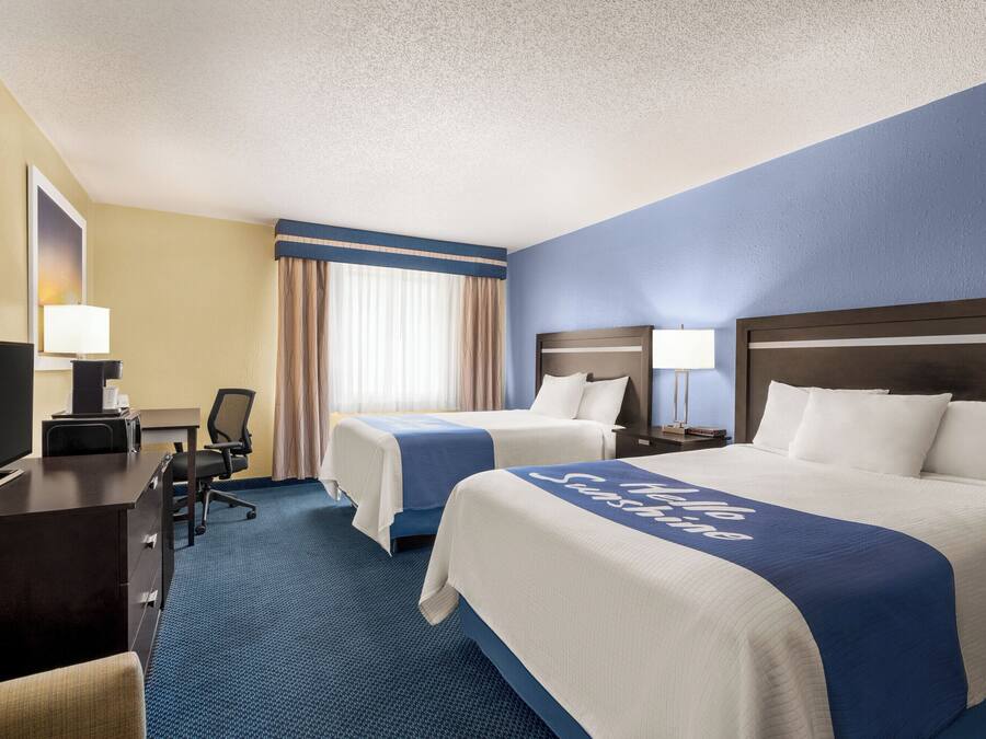 Quarto de hotel com duas camas, uma escrivaninha, uma cadeira, uma televisão e uma janela com cortinas.