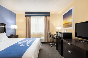 Quarto de hotel com cama, escrivaninha, televisão e uma grande janela com cortinas.