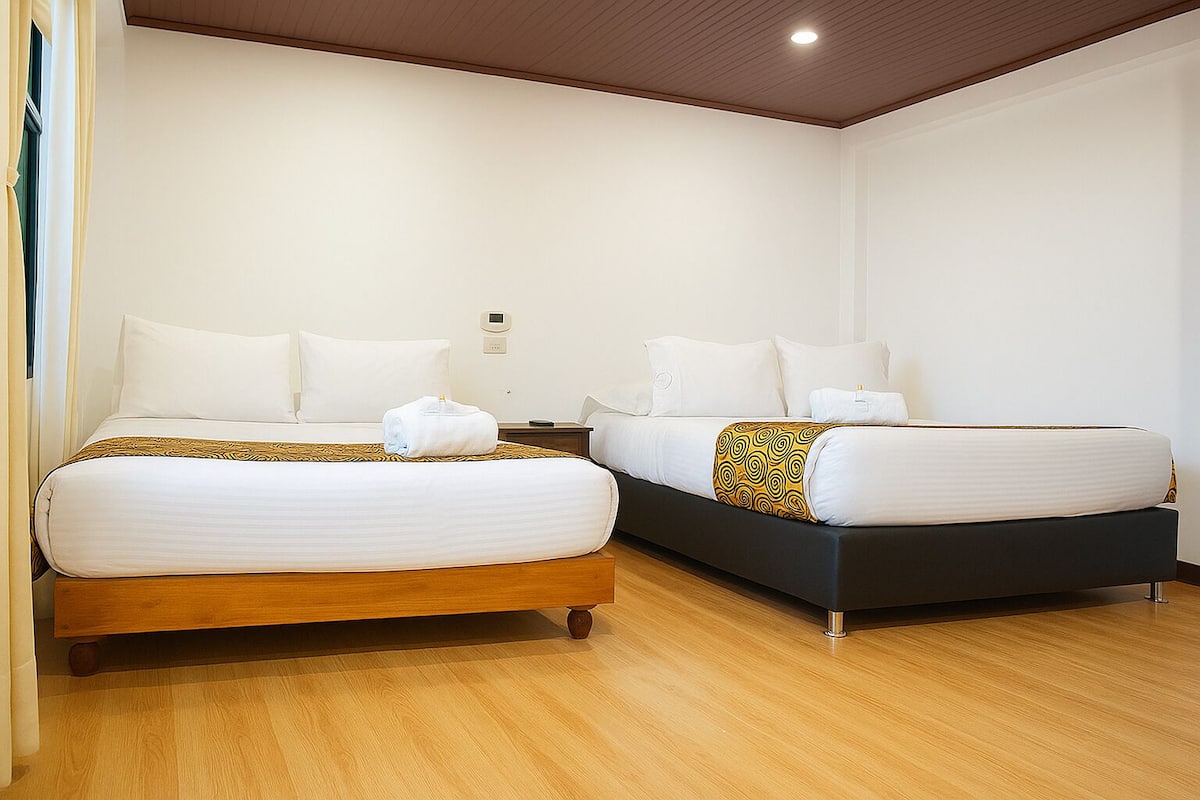 Quarto de hotel com duas camas, piso de madeira, teto de madeira e mesa de cabeceira com relógio digital.