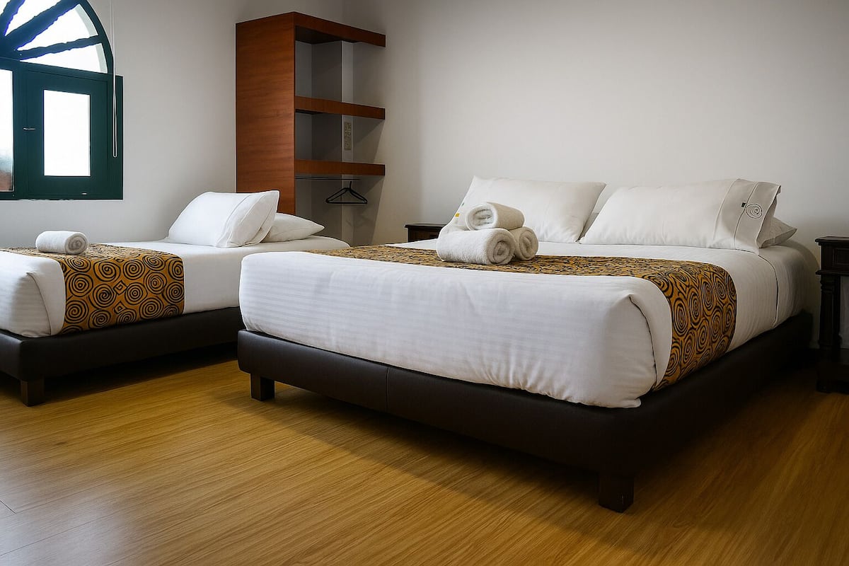 Quarto de hotel com duas camas, piso de madeira, um guarda-roupa e janela com vista.