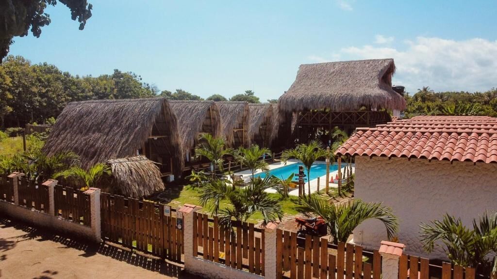 Um resort com edifícios de telhado de palha, uma piscina e palmeiras.