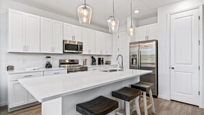 Cozinha moderna com armários brancos, eletrodomésticos de aço inoxidável, uma ilha grande com banquetas e iluminação pendente.