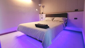 Quarto de hotel moderno com uma cama bem arrumada, uma luminária de mesa e um aplique na parede.