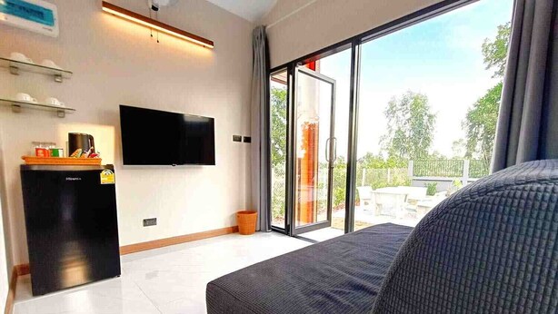Quarto de hotel moderno com uma cama grande, uma televisão de tela plana na parede, um pequeno espaço de cozinha e uma porta de vidro deslizante para uma varanda.