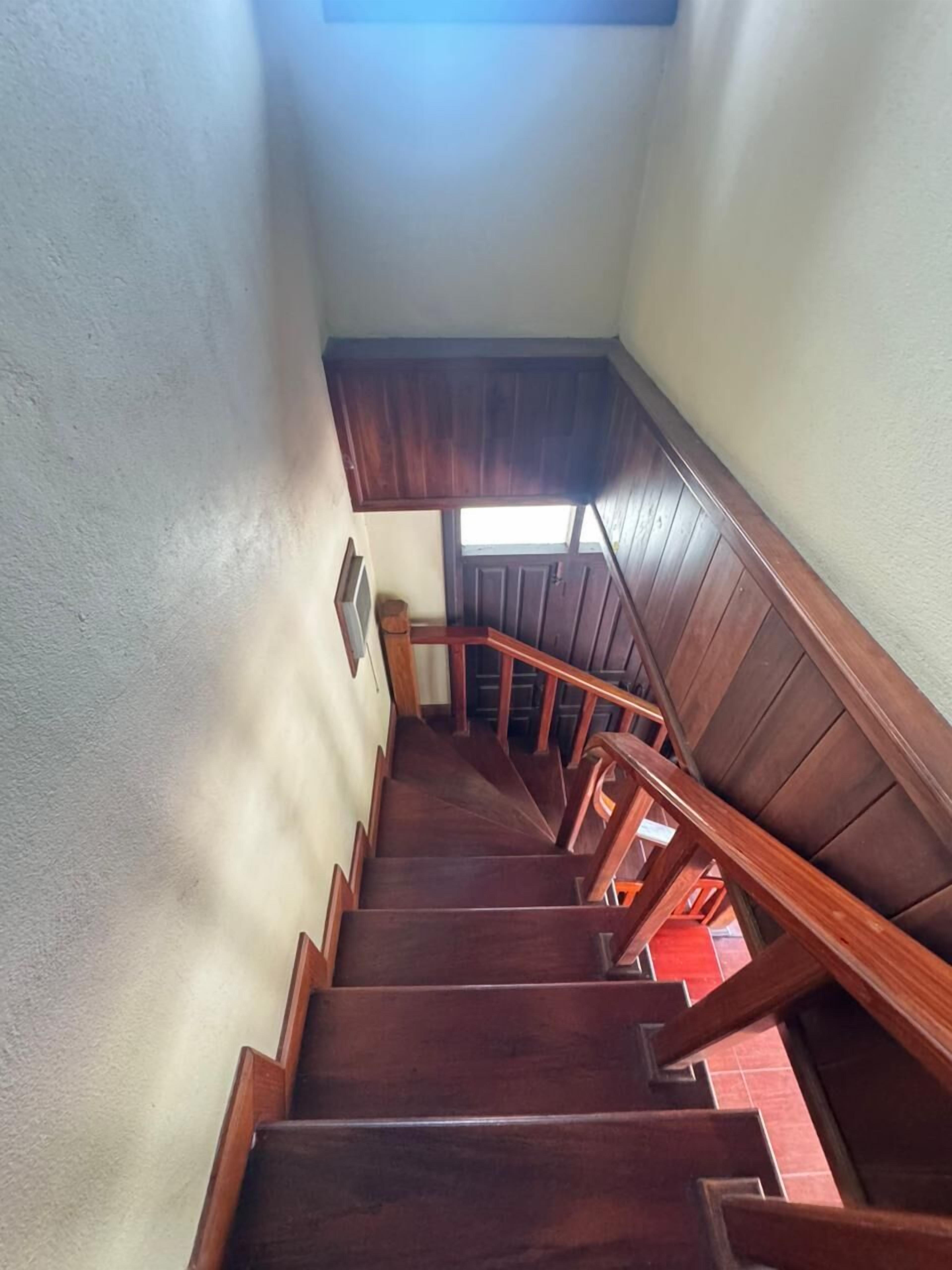 Escada de madeira com corrimão, que leva a um patamar com janela.
