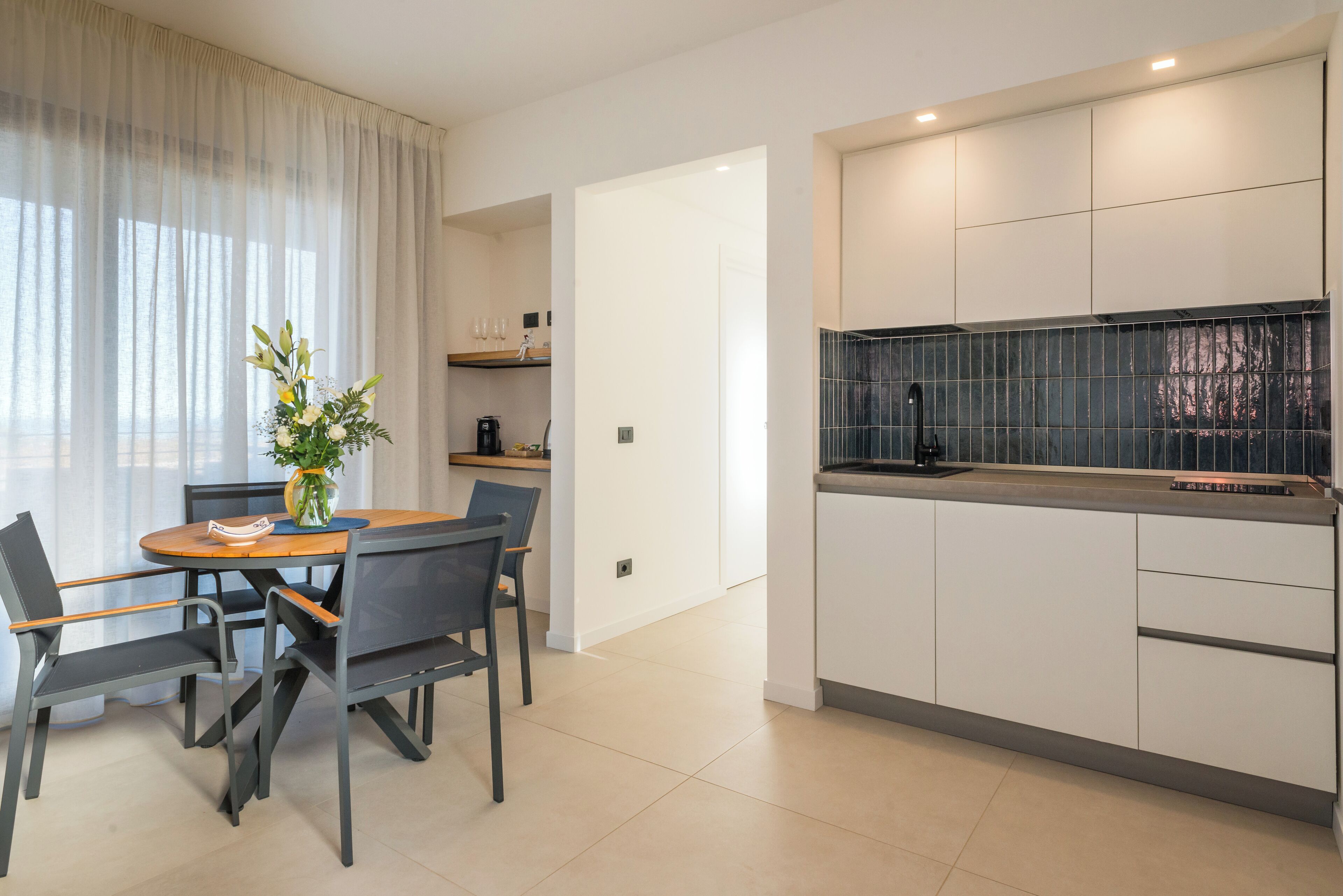 Cozinha moderna com armários brancos, painel de fundo preto e uma área de jantar com mesa e cadeiras.