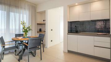 Cozinha moderna com armários brancos, painel de fundo preto e uma área de jantar com mesa e cadeiras.