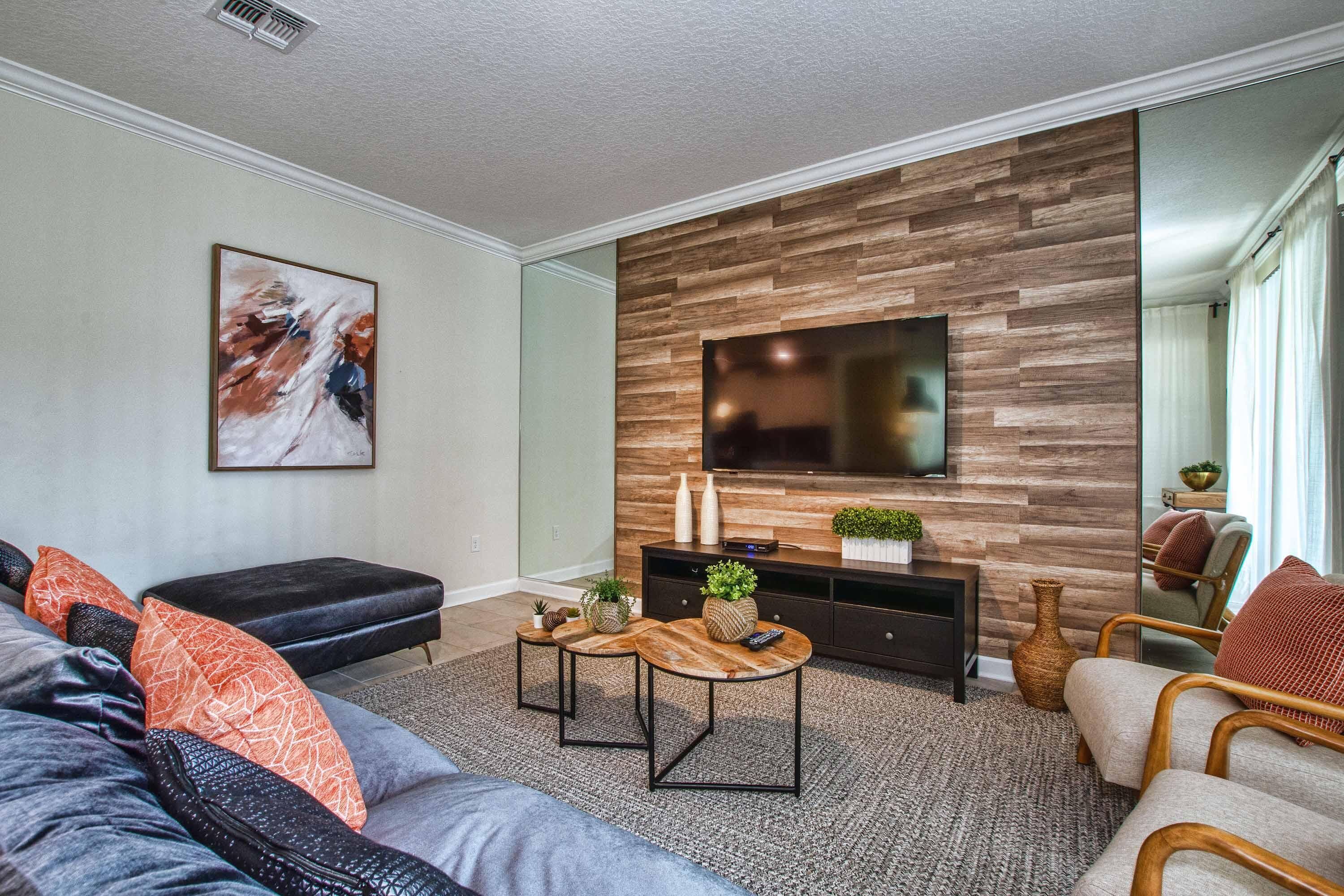 Uma sala de estar moderna com uma TV de tela plana fixada numa parede de madeira, um sofá, uma mesa de centro e uma mesinha lateral com objetos decorativos.