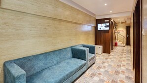 Um lobby moderno com sofá azul, carpete estampado, parede de madeira e escada com letreiro neon.