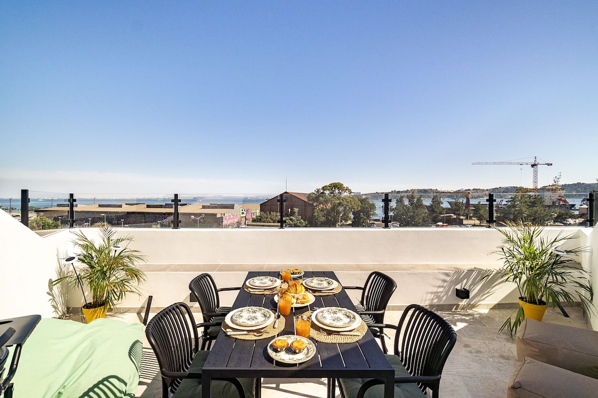 Terraço no telhado com mesa posta para refeição, com vista para a paisagem urbana e o oceano.