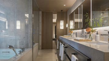 Uma casa de banho moderna com chuveiro envolto em vidro, um espelho grande e uma toucador com lavatório e porta-toalhas.