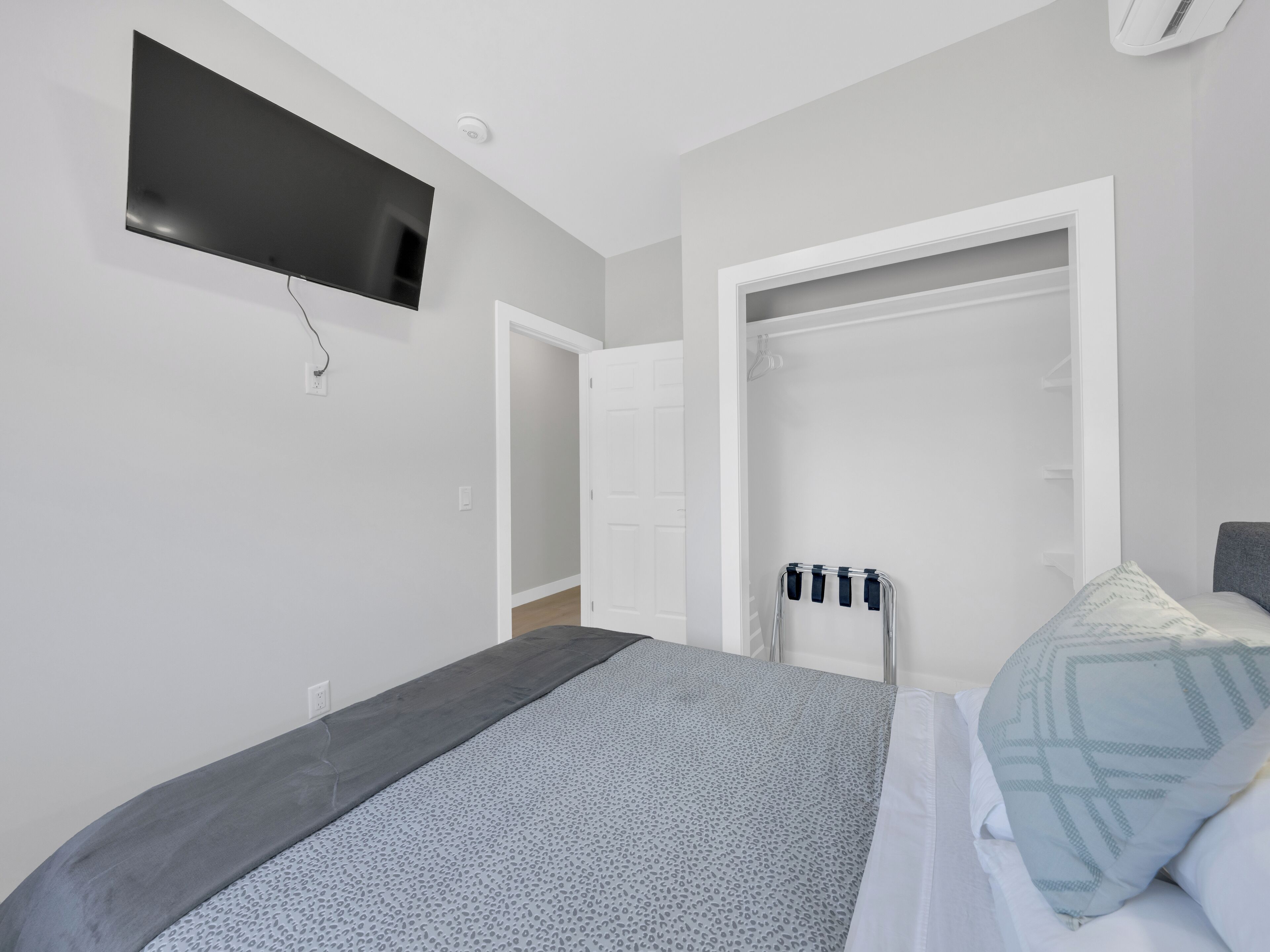 Quarto com cama, televisão na parede e guarda-roupa.