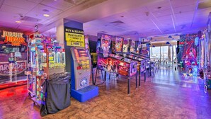 Uma área de jogos bem iluminada com diversas máquinas de jogo, uma máquina de 'Buy & Reload' e um letreiro de 'Jurassic Park'.