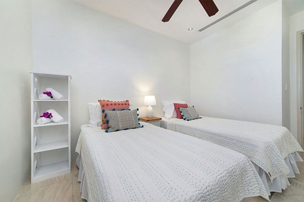 Quarto de hotel com duas camas, uma prateleira branca com toalhas e um ventilador de teto.
