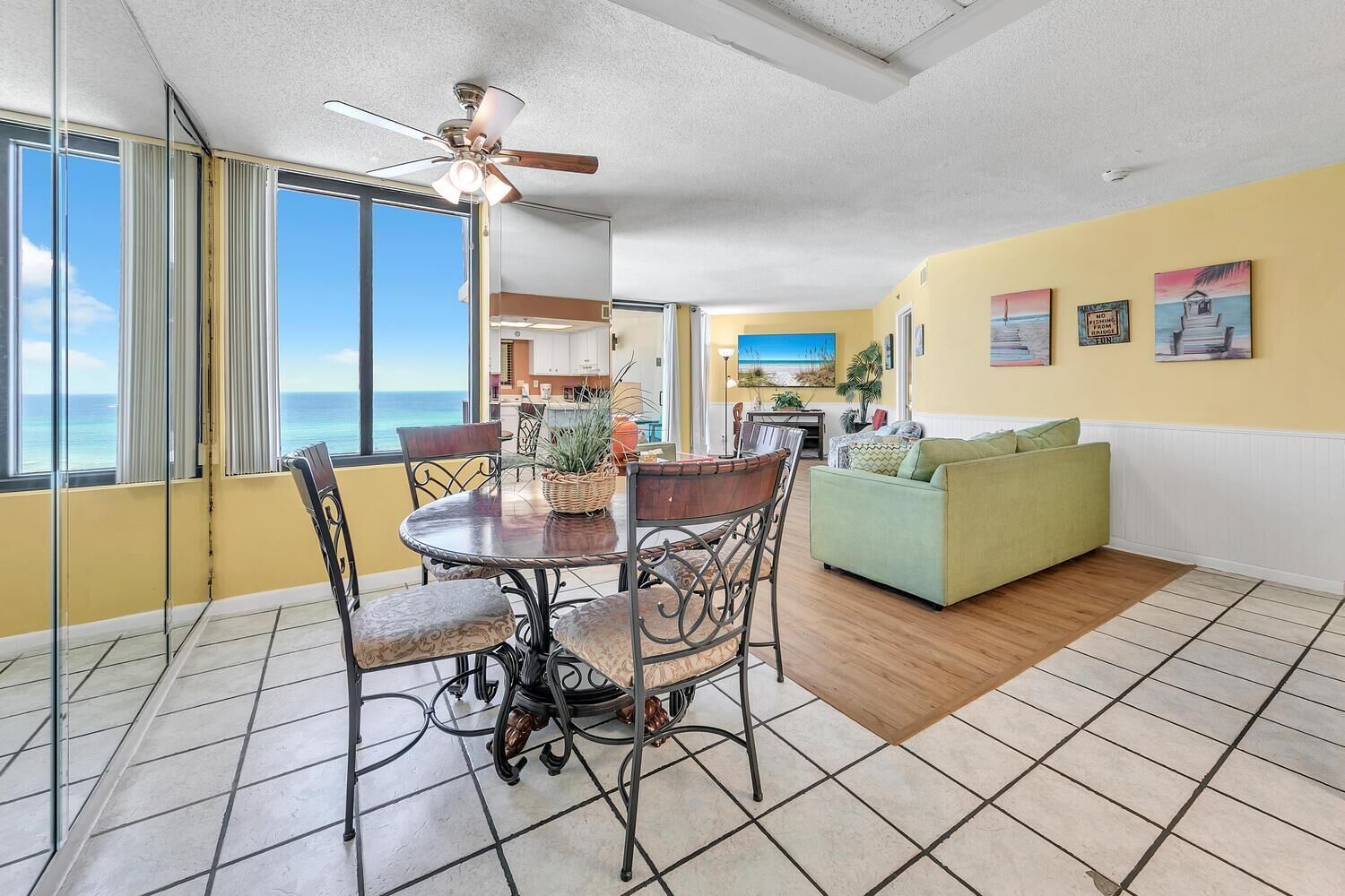 Ampla sala de estar com uma mesa de jantar, cadeiras, um sofá verde e vista para o oceano.