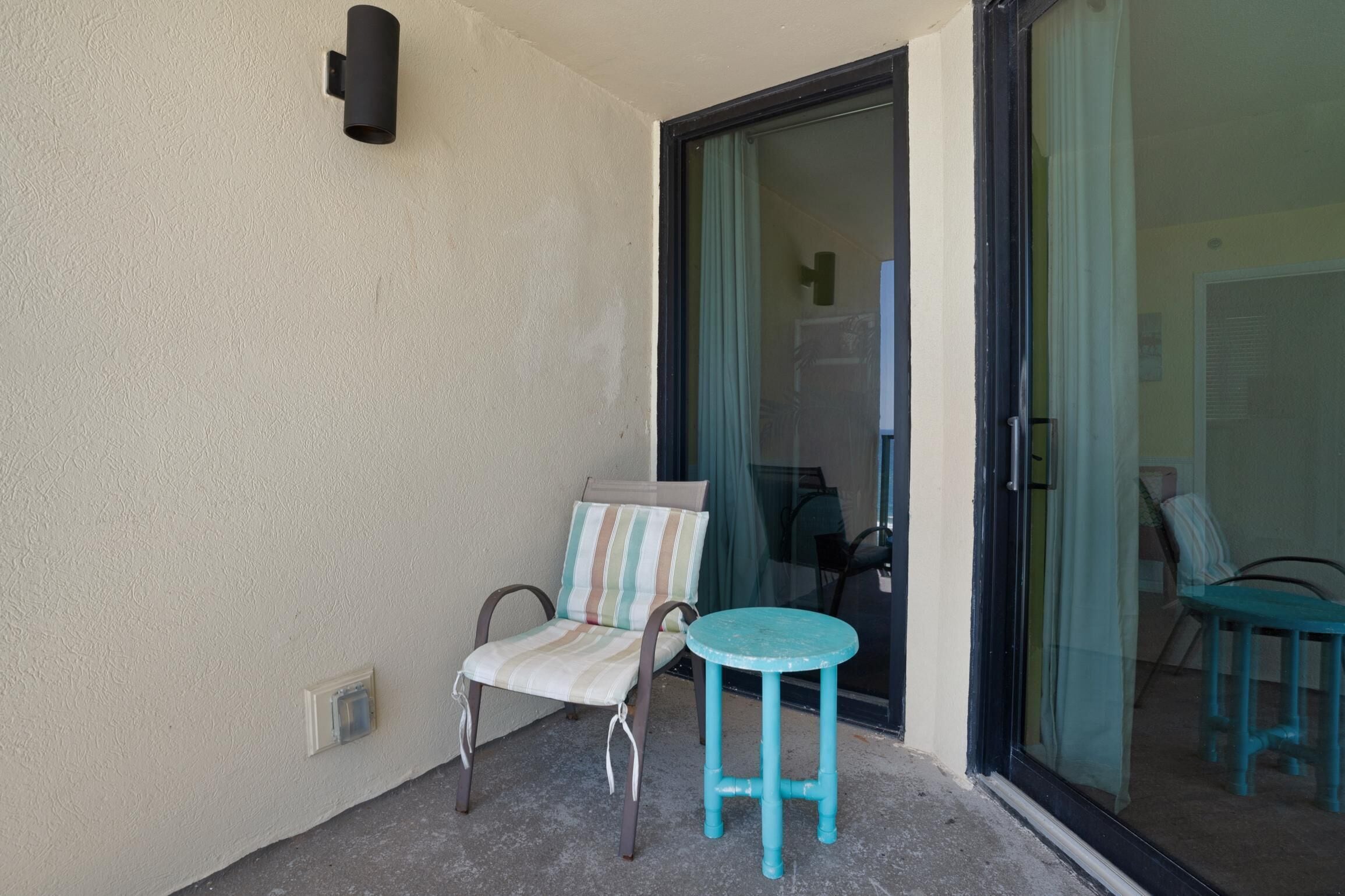 Varanda com cadeira, mesa pequena, porta de correr de vidro e vista para o interior.