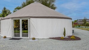Tenda branca em forma de cúpula com porta deslizante, rodeada por cascalho e pequenas plantas.
