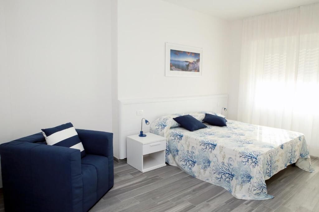 Quarto com uma cama, mesa de cabeceira, cadeira e um quadro na parede.