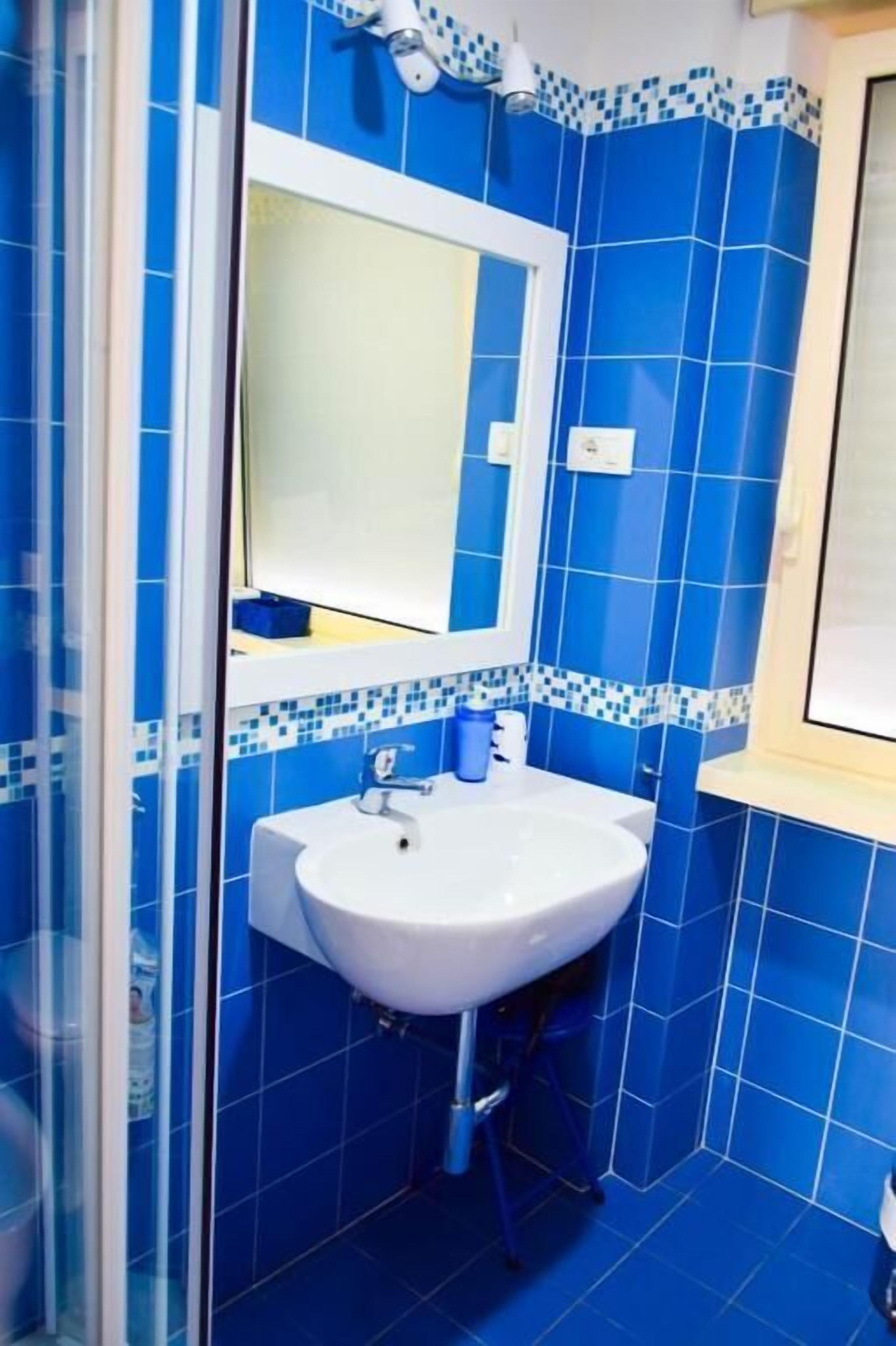 Casa de banho com azulejos azuis, uma pia branca e um espelho.