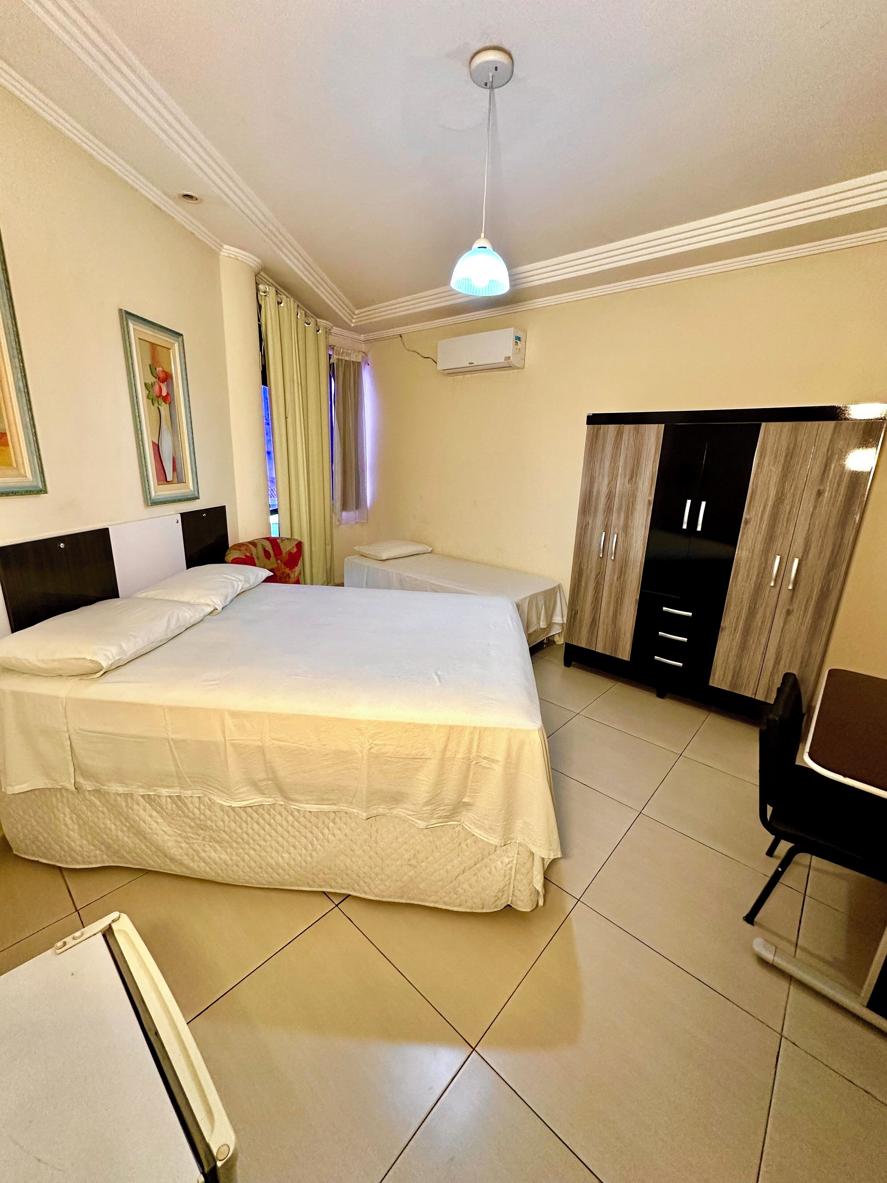 Quarto de hotel com uma cama grande, uma escrivaninha, um guarda-roupa e um aparelho de ar condicionado.