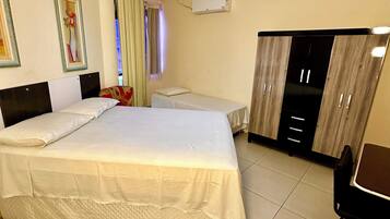 Quarto de hotel com uma cama grande, uma escrivaninha, um guarda-roupa e um aparelho de ar condicionado.