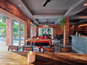 Um interior moderno com parede de tijolos, janelas amplas, área de estar com almofadas vermelhas e um balcão de bar.
