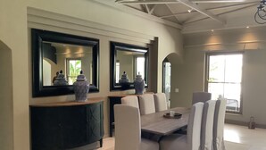 Uma área de refeições com uma mesa comprida, cadeiras acolchoadas e vasos decorativos.