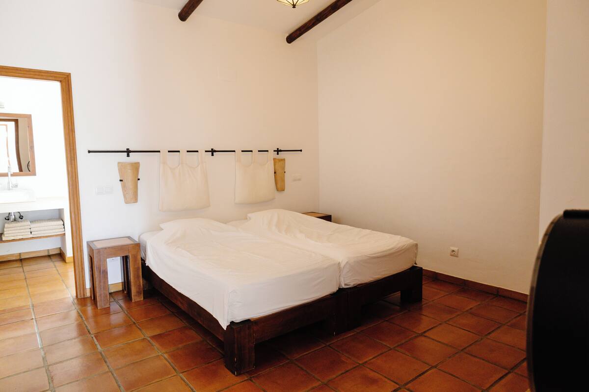 Quarto com cama de madeira, uma mesinha de cabeceira e prateleira na parede com toalhas.
