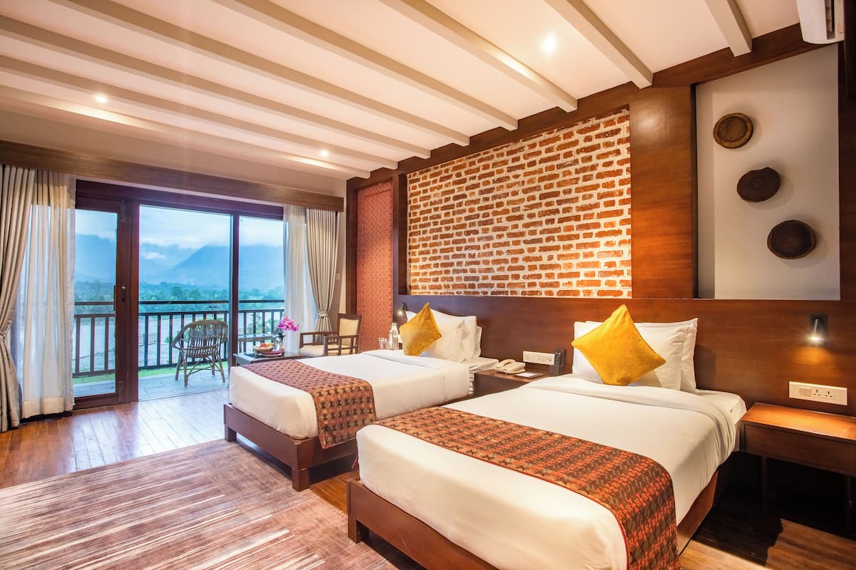 Quarto de hotel com duas camas, varanda com vista e parede de destaque em tijolo.