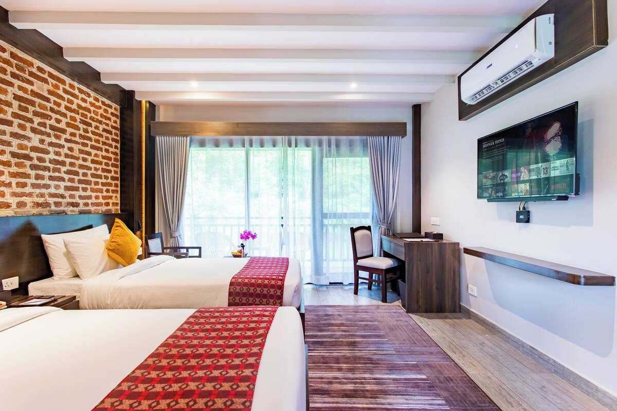 Quarto de hotel com duas camas, televisão, escrivaninha e parede de tijolos.