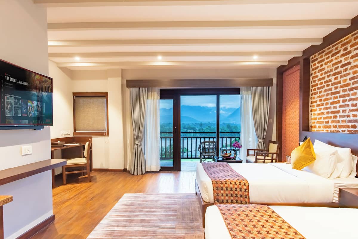 Quarto de hotel com cama, escrivaninha, cadeira e varanda com vista para as montanhas.