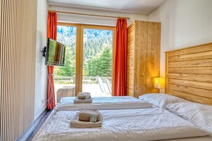 Quarto de hotel com duas camas, televisão e vista para árvores pela janela.
