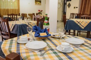 Uma sala de jantar com toalhas de mesa xadrez, mesas bem arrumadas com pratos, copos e uma garrafa de Lete.