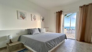 Um quarto com uma cama, mesa de cabeceira, abajur, janela com cortinas e uma obra de arte na parede.