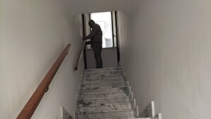 Uma escadaria de mármore com guarda-corpo de madeira que leva a uma porta no topo.
